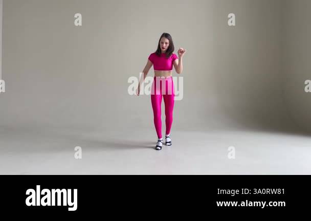 Woman performing salsa in a vibrant pink costume against a neutral gray ...