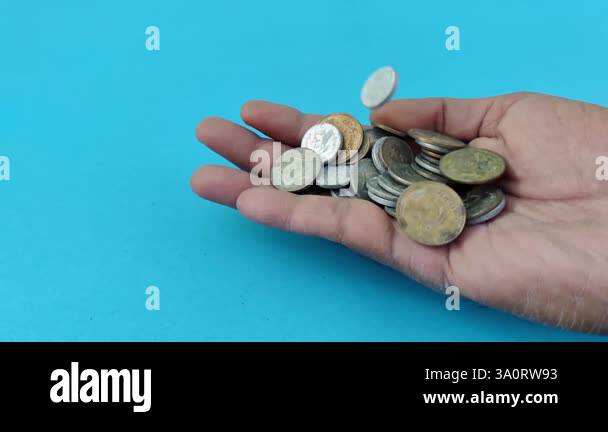 A hand holds scattered coins while more fall from above, some slipping ...