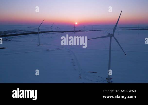 Aerial view of a wind farm in a snowy landscape at sunset. Large wind ...