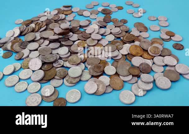 A pile of coins rests on a light blue background while additional coins ...