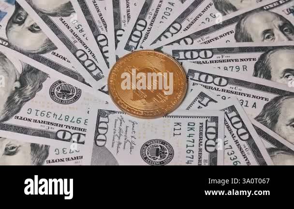 A gold Bitcoin coin sits atop a fan of one hundred dollar bills ...