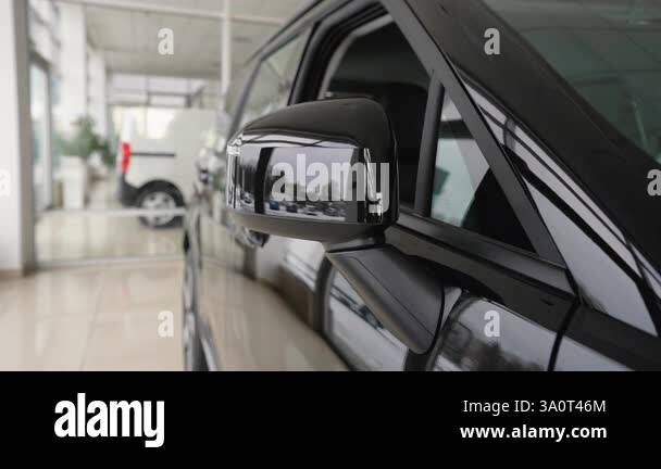 Close-up of a folding side mirror on a sleek black car in a dealership ...