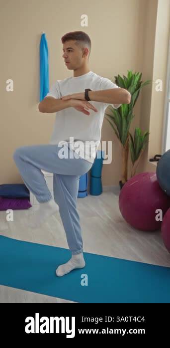Young man balancing on one foot indoors at a gym, focusing during his ...