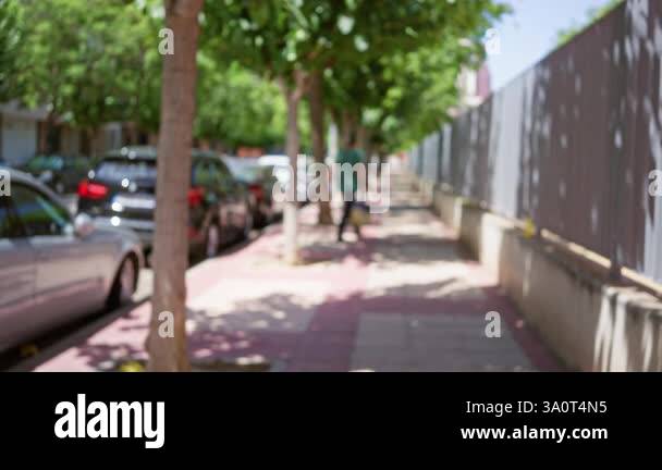 Blurry image of an outdoor street scene with cars parked alongside a ...