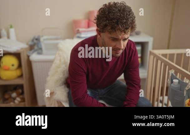 Young man sits in bedroom by cradle looking thoughtful and emotional ...