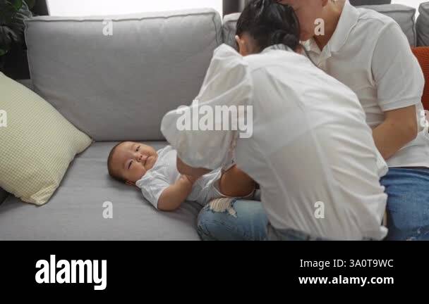 Parents changing baby's diaper on living room sofa, displaying caring ...