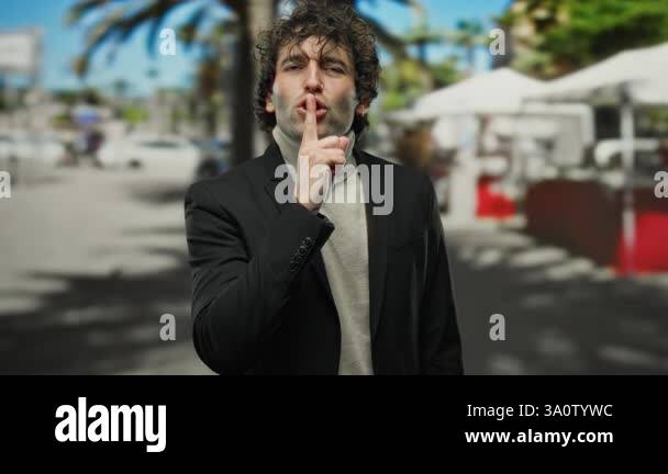 Young man in city street outdoors making a shushing gesture with finger ...