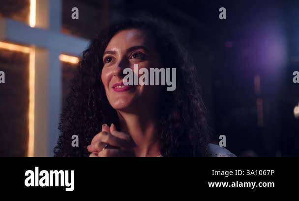 Young woman smiling during prayer in a church, hands clasped, glowing ...