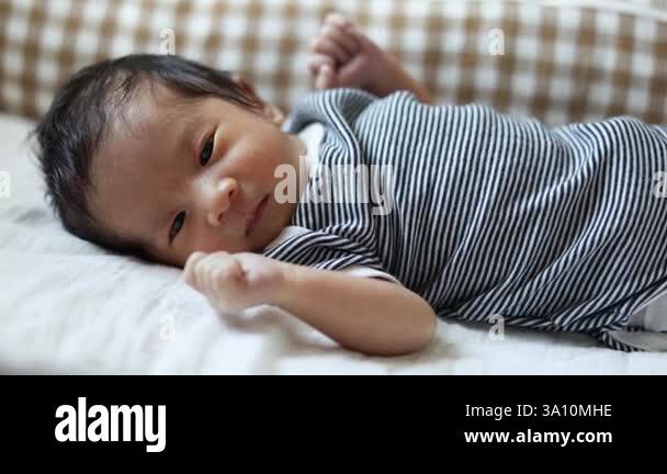 A baby is laying on a white sheet with its arms outstretched. The baby ...