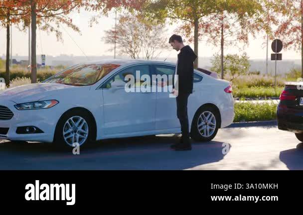 Young man approaches a luxurious white car with his phone in his hand ...
