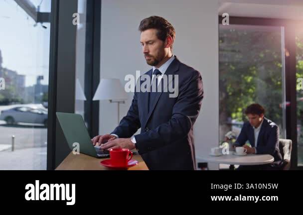 Businessman typing laptop in cafeteria enjoying hot coffee. Thoughtful ...