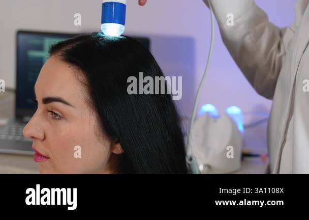 A trichologist performs a scalp examination on a woman using a digital ...