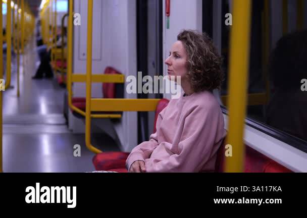 Young woman sitting on subway train, gazing contemplatively through window during routine ...