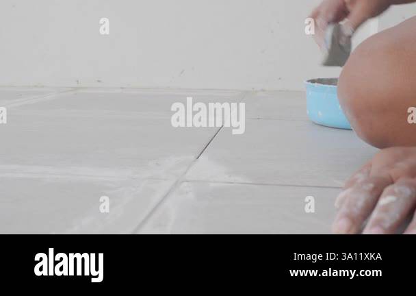 A hand with a rubber trowel smoothing mortar between gray ceramic floor ...
