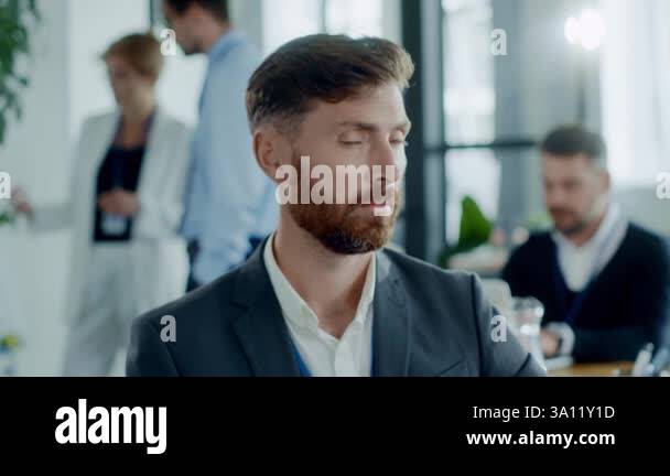 A male presenter with a beard engages an audience in a modern office ...