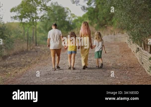 Happy family walking away from the viewer on a path holding hands Stock ...