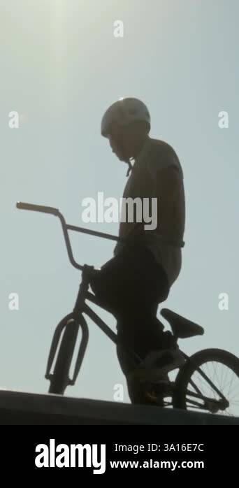 Vertical low angle shot of silhouetted BMX rider wearing helmet and ...