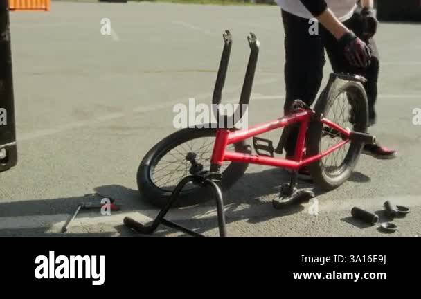 Young BMX rider using tools to adjust wheel and pegs while fixing bike ...