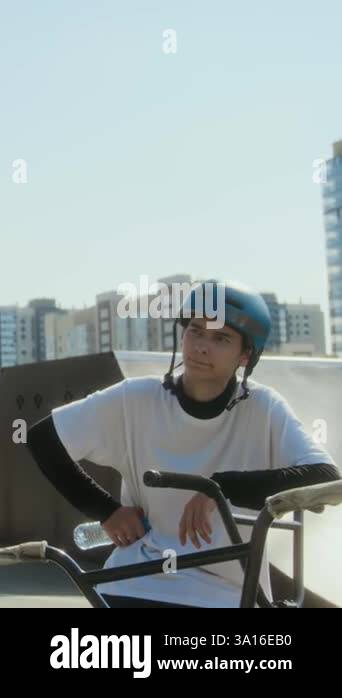 Vertical shot of young BMX rider in helmet leaning on bike handlebars ...