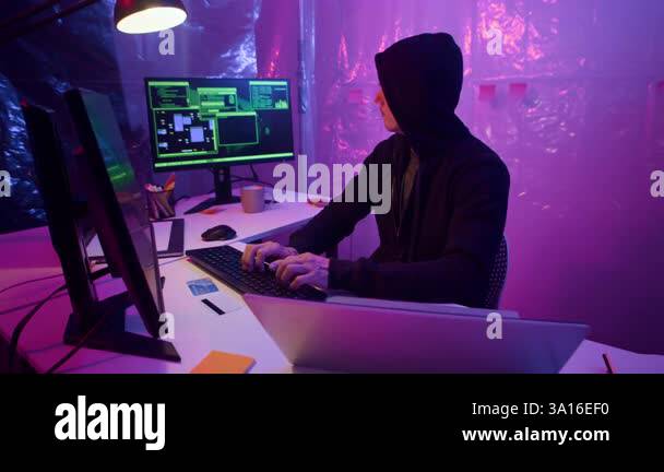 Medium low key shot of male cybercriminal sitting in dark room with ...