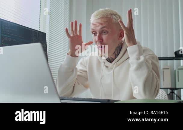 Medium shot of happy Caucasian tattooed man sitting in front of laptop screen while working with ...