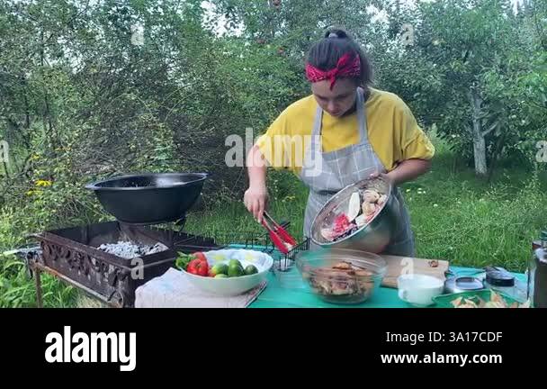 A young beautiful woman in an apron prepares food outdoors, cooking ...