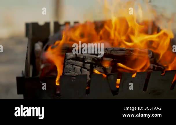 Flames dance in a barbecue grill set on the lakeshore. Firewood burns ...