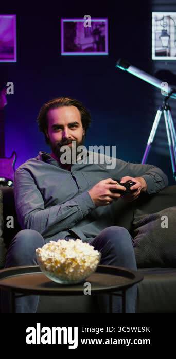 Vertical video Cheerful gamer sitting on couch engaging in online ...