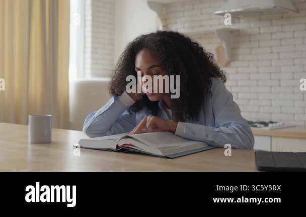 Young Woman Reading Book At Home, Resting Her Head On Hand, Deeply ...