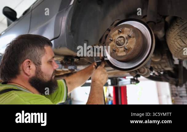 Professional bearded auto mechanic in uniform repairs detail of car ...