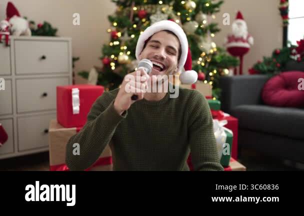 Happy handsome young man singing in the living room with a christmas ...