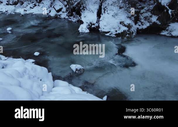 Water stream flowing under ice in mountain forest during extreme cold ...