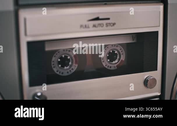 A hand loads a clear audio cassette into a vintage silver cassette ...