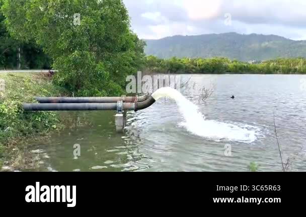 Water flows from a large metal pipe into a natural reservoir as part of ...