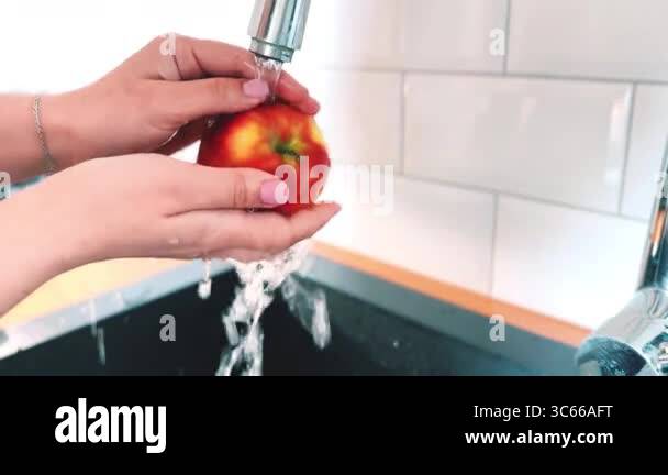Womens hands wash an apple under water in a sink. Washing red apples in ...