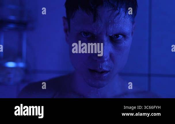 A wet man in a blue-lit shower stares intensely, water dripping from ...