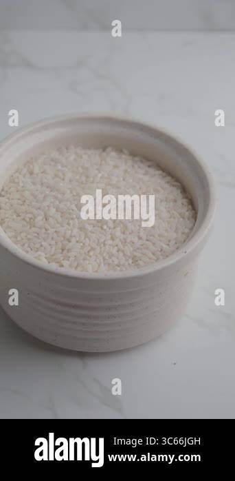 A bowl filled with uncooked rice placed on a marble countertop Stock ...