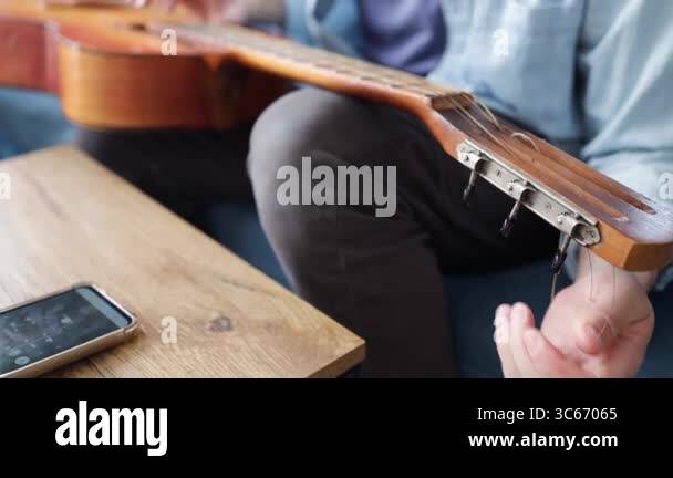 Close-up man tunes acoustic guitar and uses online smartphone ...