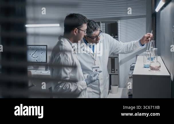 Side through-glass shot of male senior professor teaching young lab ...