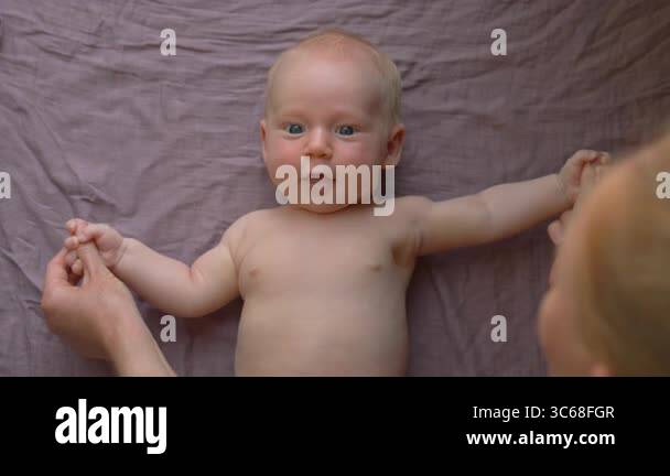 A mother gently performs newborn gymnastics with her tiny baby, softly ...