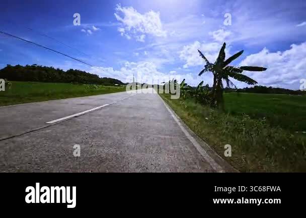 A straight concrete road stretches endlessly through lush green fields ...