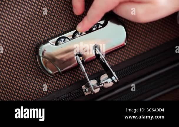 A hand meticulously sets the combination lock on the suitcase, securing ...