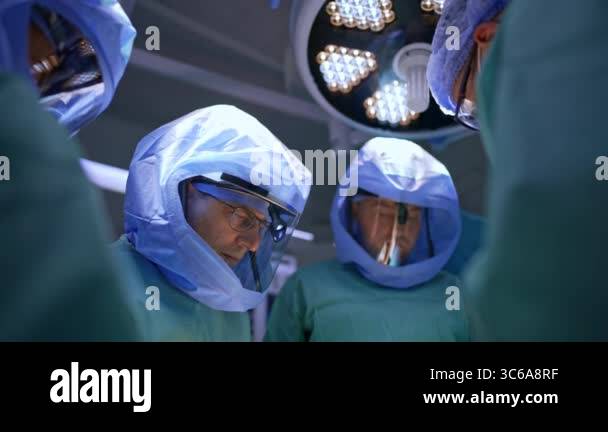 Doctors surrounding operating table wear protective helmets at ...