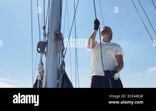 Male captain on deck of sailboat opening sails pulling the rope Stock ...