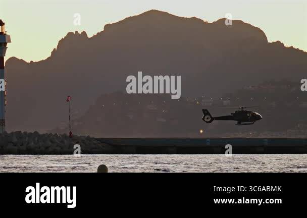 View of a helicopter landing at sunset near a lighthouse with the ...