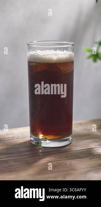fresh sparkling cola drink in a glass on sunny wooden kitchen tabletop ...