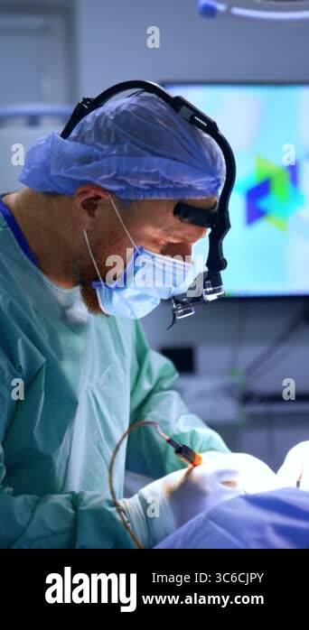 Mature male Caucasian surgeon leaned over the patient using tool device ...