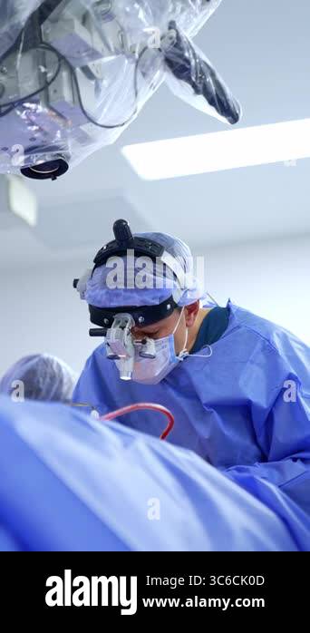 Professional male Caucasian surgeon in surgical loupes leaning above ...