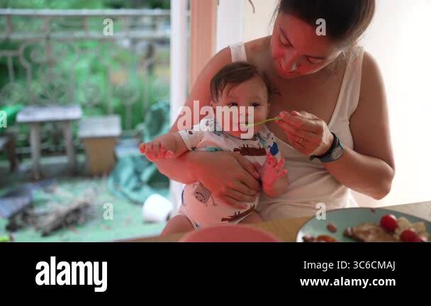 Mother feeding baby first solid food, baby biting vegetable, early food exploration, baby-led ...