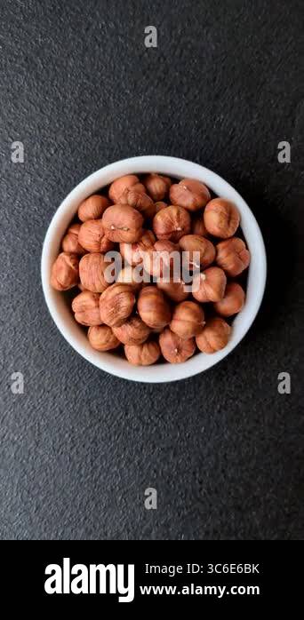 Raw hazelnuts without shells in a bowl on a dark concrete background ...